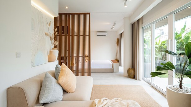 Quarto de hotel moderno com uma cama grande, um sofá, uma janela ampla com vista para vegetação e uma peça decorativa na parede.
