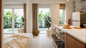 Cozinha moderna com bancada branca, banquetas e uma grande janela com vista para um jardim.