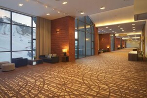 Um saguão de hotel com carpete estampado, área de estar, janelas amplas e vista para uma paisagem nevada.