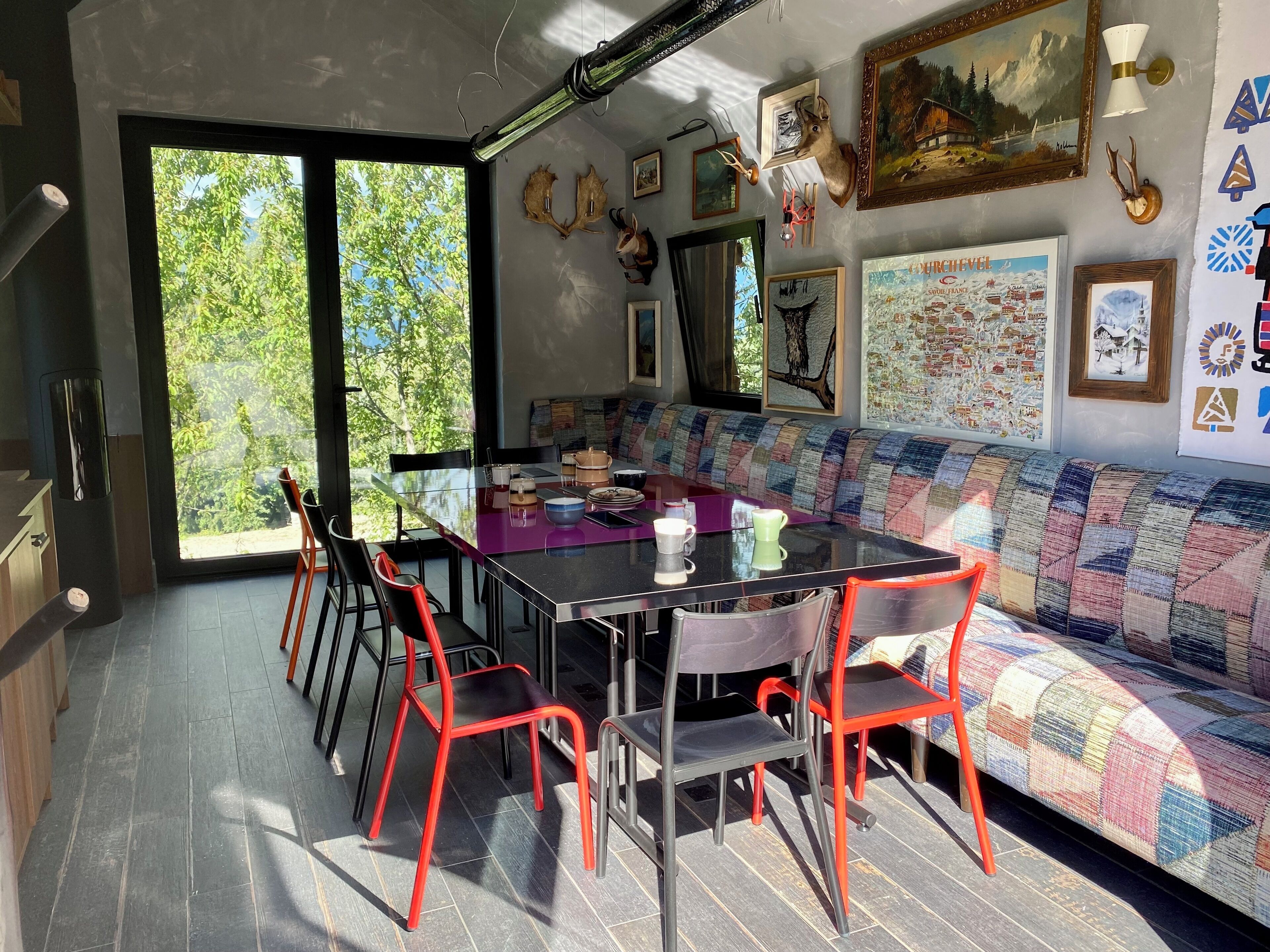 Uma zona de refeições moderna com mesa de vidro, cadeiras vermelhas e um sofá acolchoado e colorido.