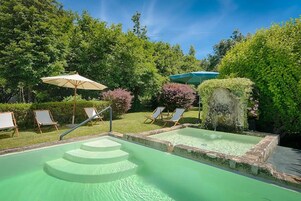 Piscina com degraus de acesso, cercada por vegetação e duas espreguiçadeiras.