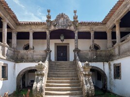 Um edifício histórico com uma escadaria central, portas em arco e telhado em azulejos.