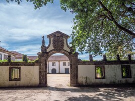 Uma entrada com um arco ornamentado que dá para um pátio com edifícios ao fundo.