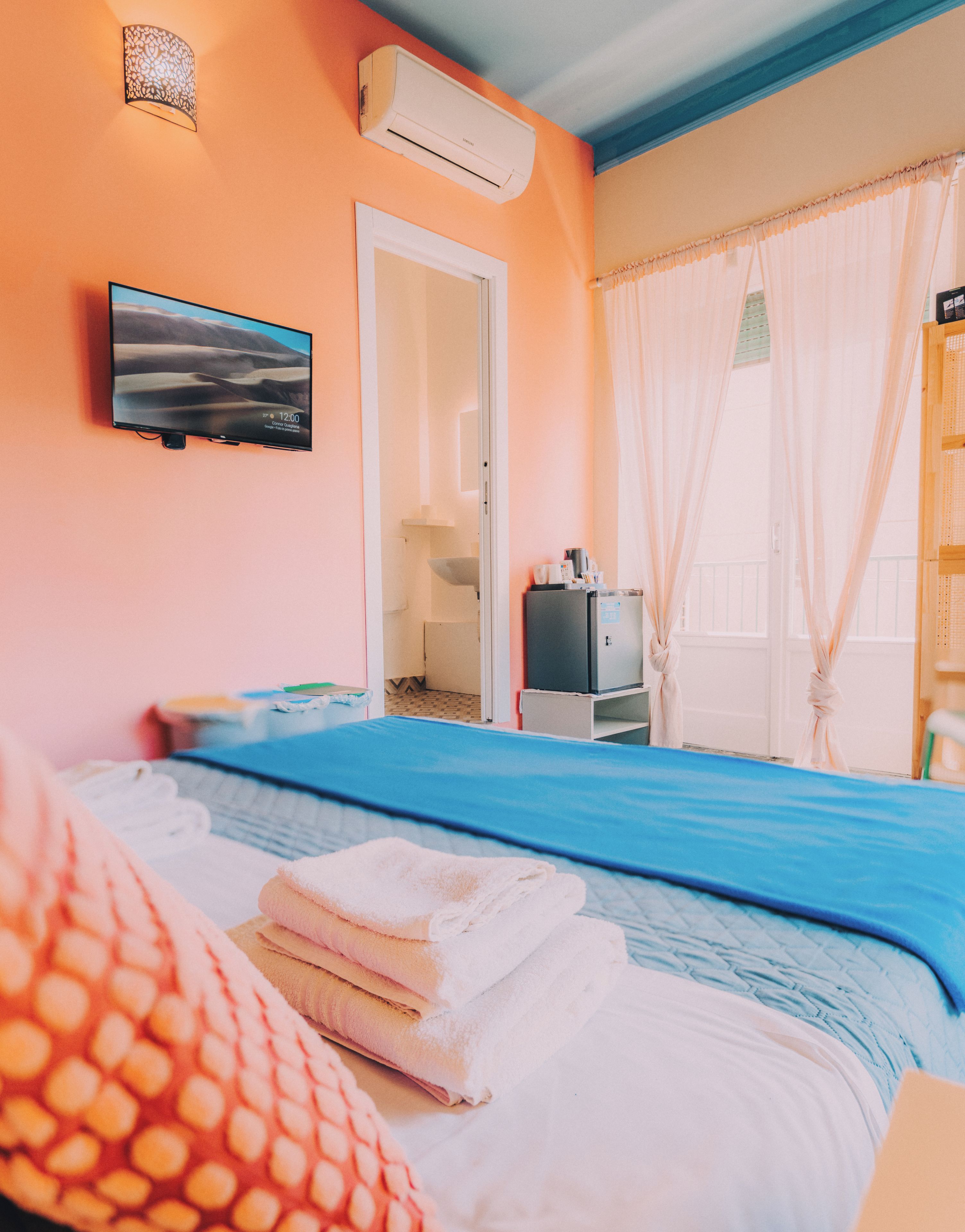 Quarto com cama, televisão, ar condicionado e janela com cortinas.