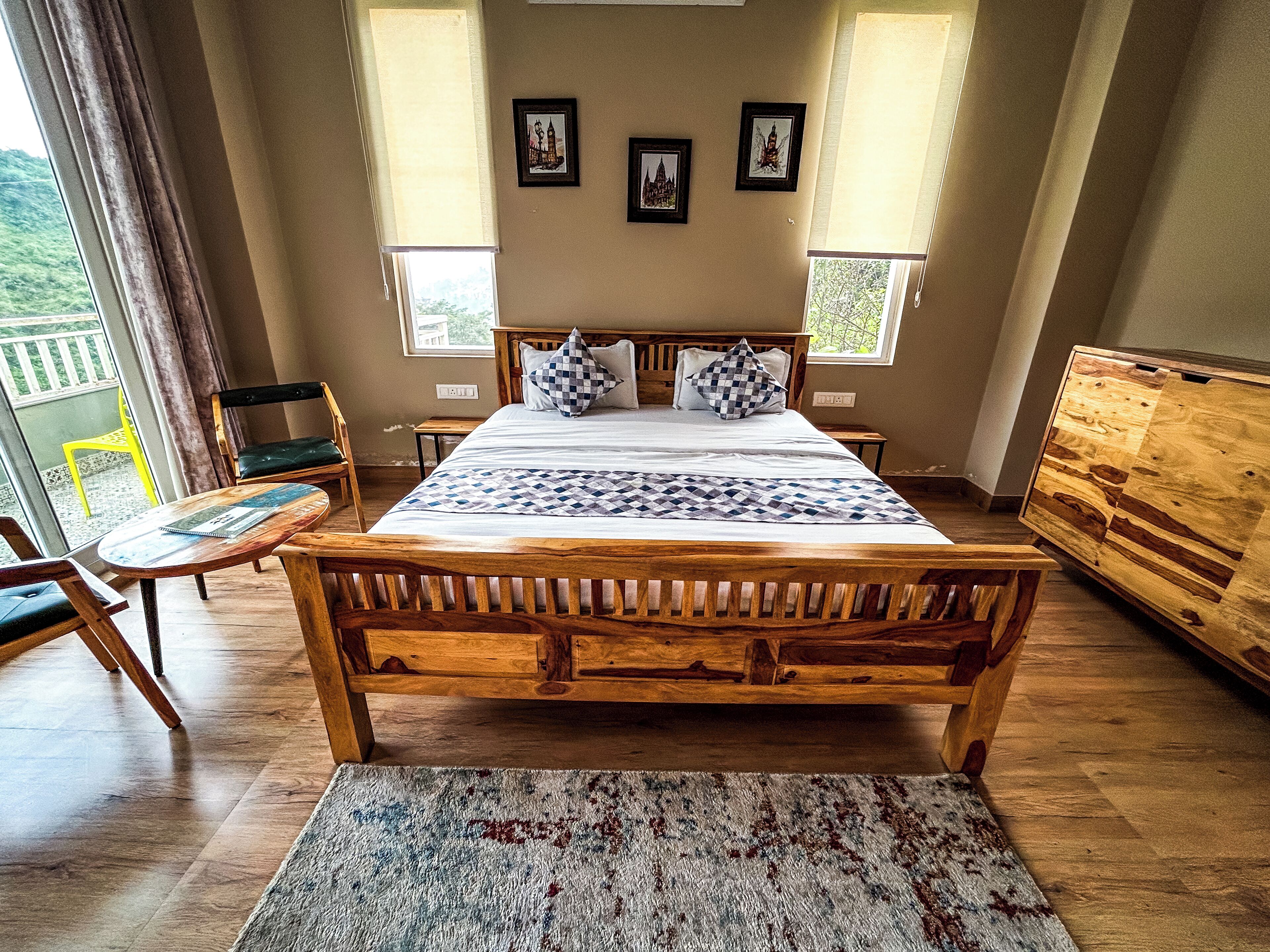 Quarto com cama de madeira, uma mesinha, cadeiras e vista para o verde lá fora.