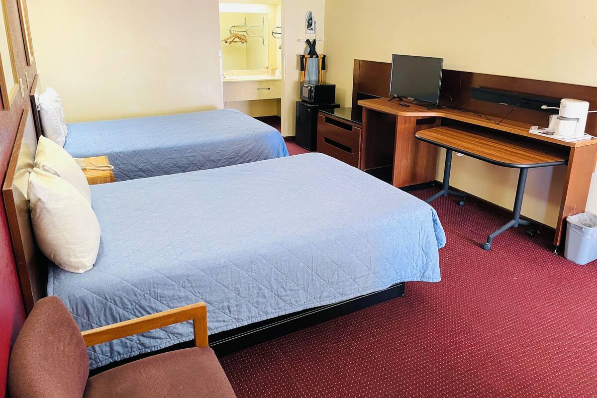 Quarto de hotel com duas camas, uma escrivaninha, uma cadeira, televisão e máquina de café.