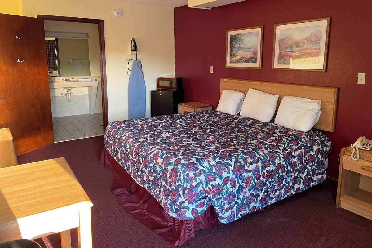 Quarto de hotel com cama, mesa de cabeceira, telefone, micro-ondas e um pequeno armário.