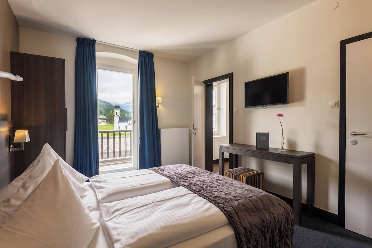 Quarto de hotel com uma cama, uma escrivaninha, uma televisão e vista para o exterior.