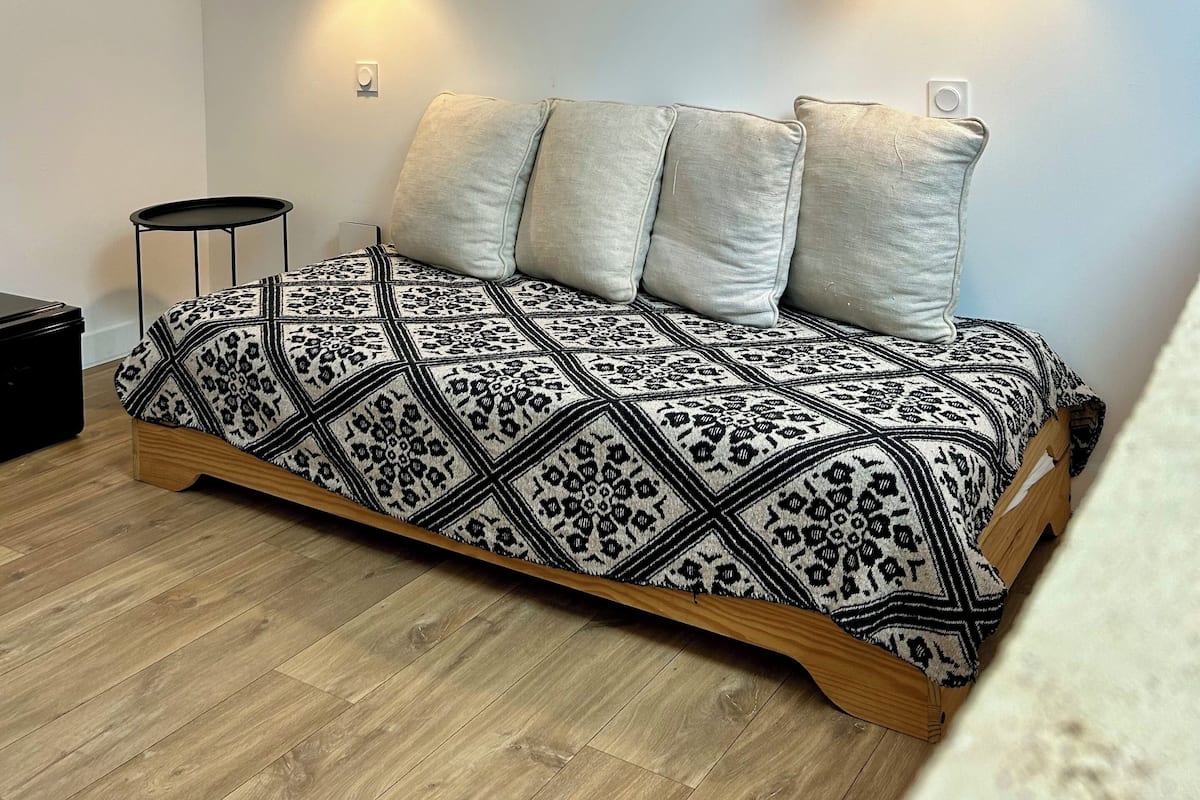 Quarto moderno com colcha estampada, luminária pendente redonda e pequena mesa de cabeceira preta.