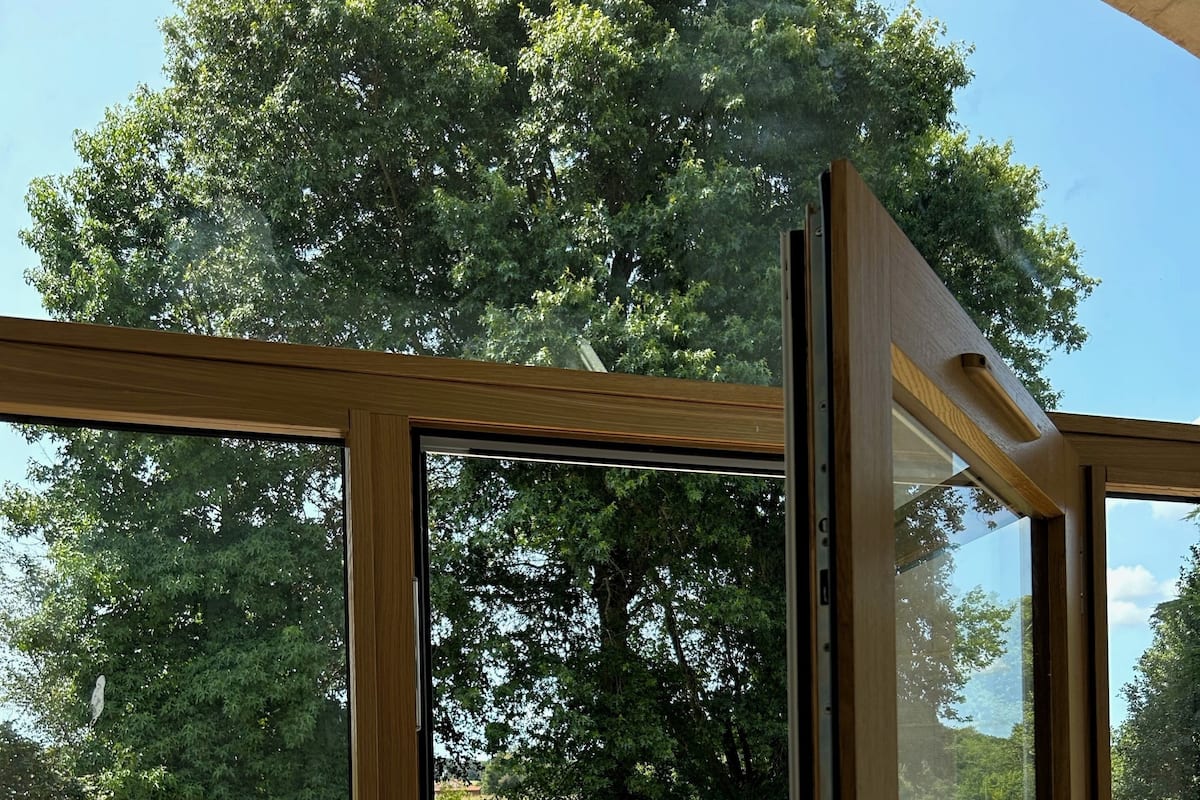 Um deck de madeira com uma porta de vidro que dá para uma área gramada com árvores.