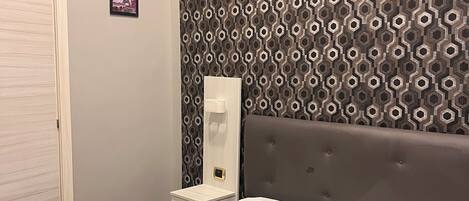 Quarto com cama, mesa de cabeceira, espelho e parede estampada.