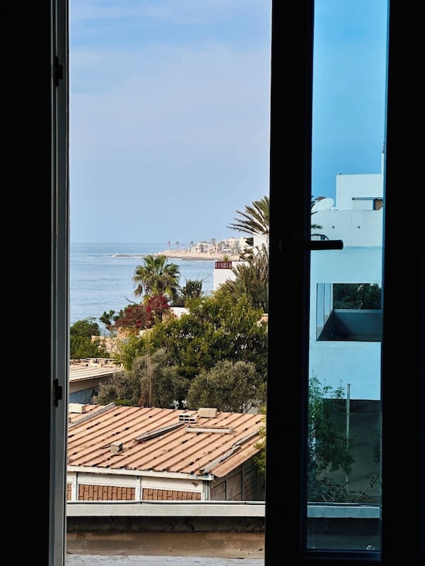 Vista costeira de uma janela com praia, palmeiras e edifícios.