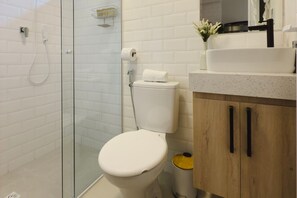 Um banheiro moderno com box de vidro, vaso sanitário branco e armários de madeira.