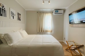 Quarto com cama, televisão fixada na parede, janela com cortinas e radiador.