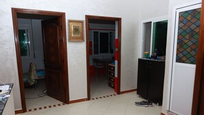 Um corredor com porta de madeira, pequena cozinha e um tapete vermelho na entrada.
