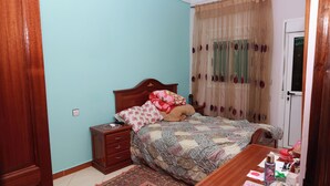 Quarto com cama, mesa de cabeceira e um pequeno armário de madeira.