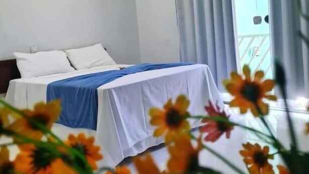 Quarto com cama, paredes brancas e janela com cortinas.