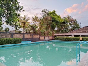 Piscina com deck de madeira, cercada por vegetação exuberante e uma parede de pedra.