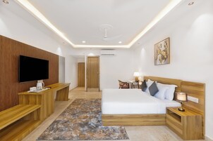 Quarto de hotel moderno com uma cama de madeira, televisão de tela plana, escrivaninha e mesa de cabeceira com luminária.