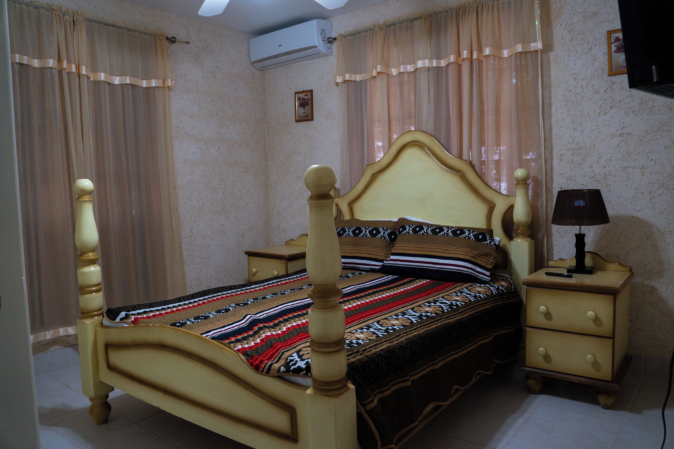 Quarto com cama, cortinas, mesa de cabeceira e ar condicionado.