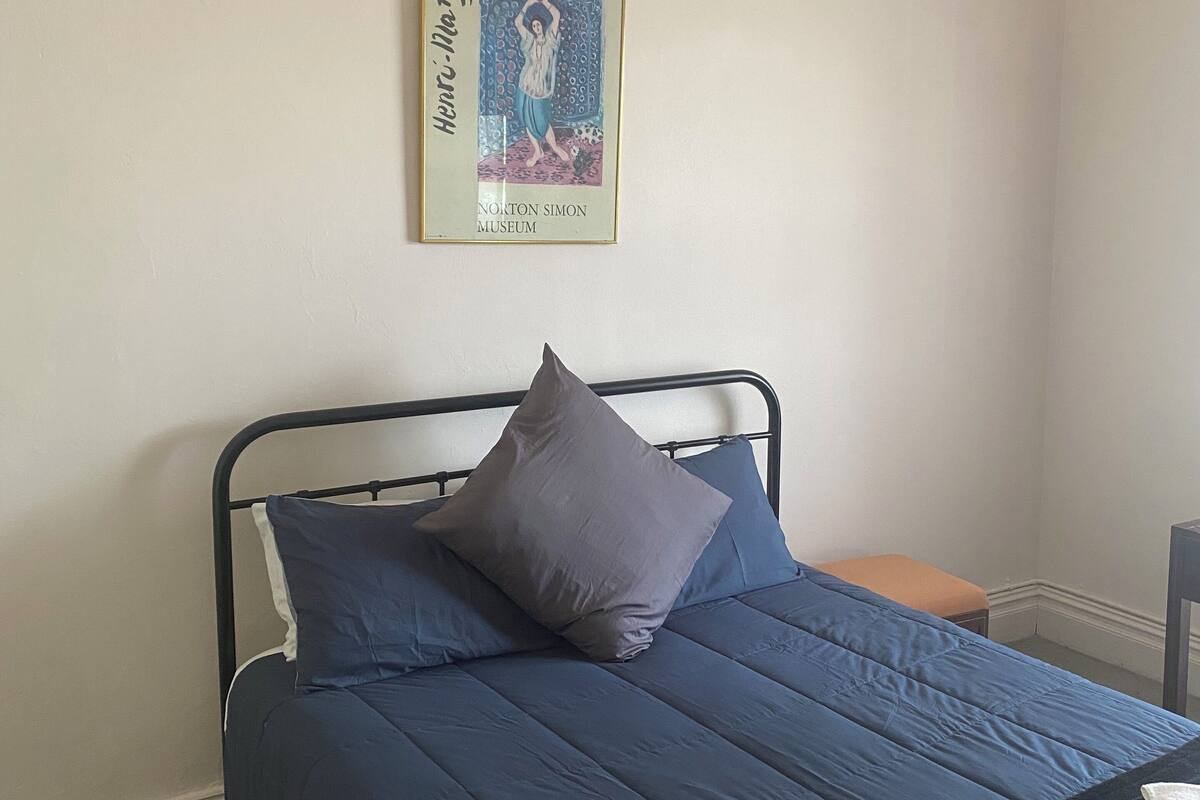Quarto com cama, travesseiro, mesa de cabeceira e um quadro na parede.