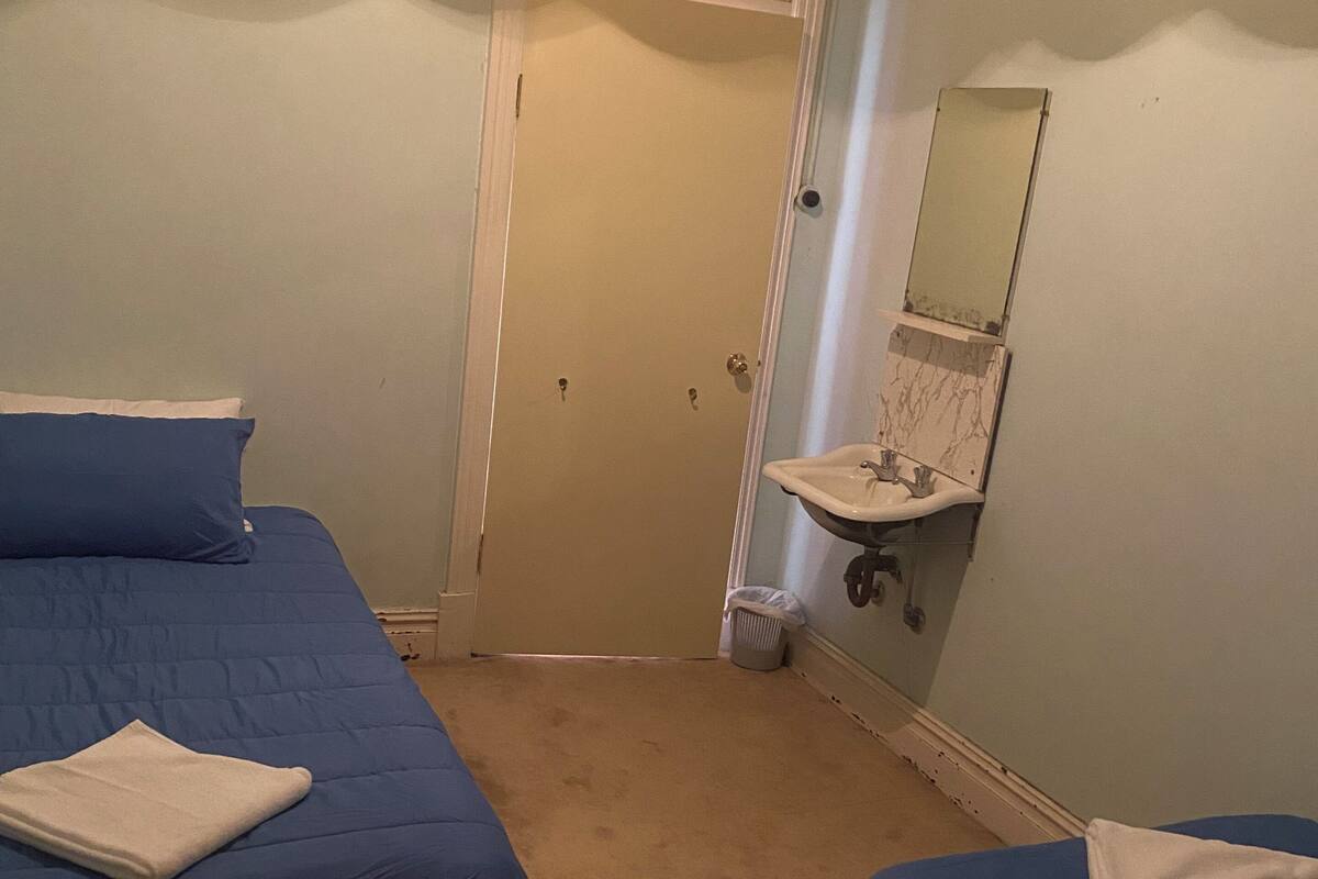 Quarto com duas camas, uma porta, uma pia e um espelho.
