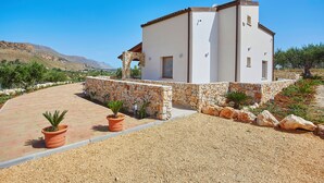 Uma casa moderna de dois andares com fundação de pedra e telhado plano, cercada por um caminho de cascalho e plantas em vasos.