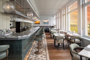 Um restaurante moderno com um balcão comprido, banquetas acolchoadas e vista para o pôr do sol através de grandes janelas.