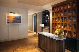 Uma área de bar com um armário de madeira repleto de garrafas, bancada de mármore e um quadro na parede.