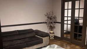 Sala de estar com um sofá marrom escuro, tapete estampado, um vaso com flores e uma porta de vidro deslizante.