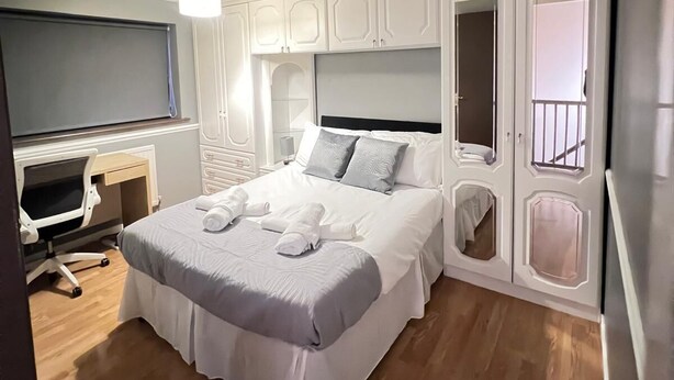 Um quarto com cama, escrivaninha e uma cadeira.