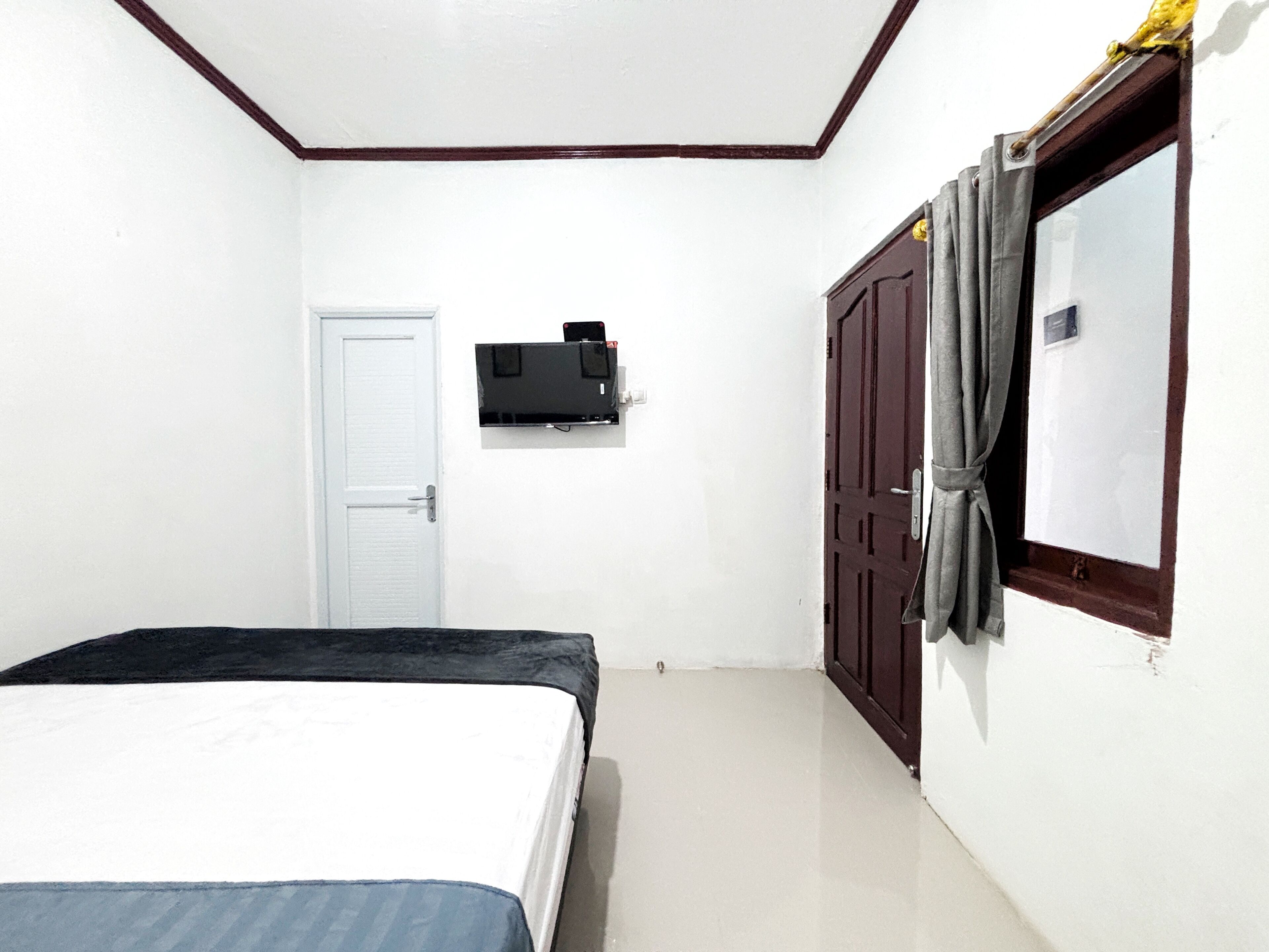 Quarto com cama, guarda-roupa, porta e televisão fixada na parede.