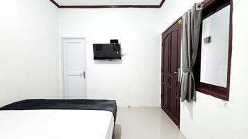 Quarto com cama, guarda-roupa, porta e televisão fixada na parede.
