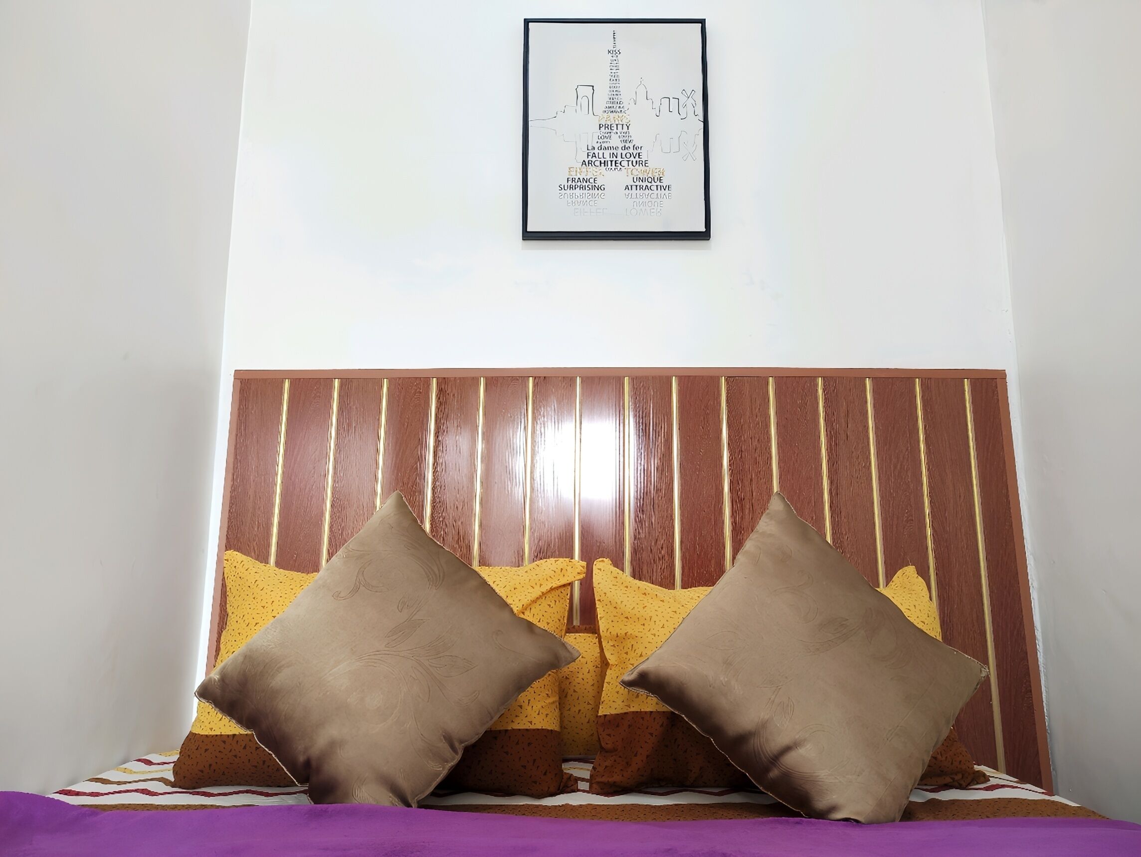 Uma cama com cabeceira listrada, duas almofadas e um quadro na parede.