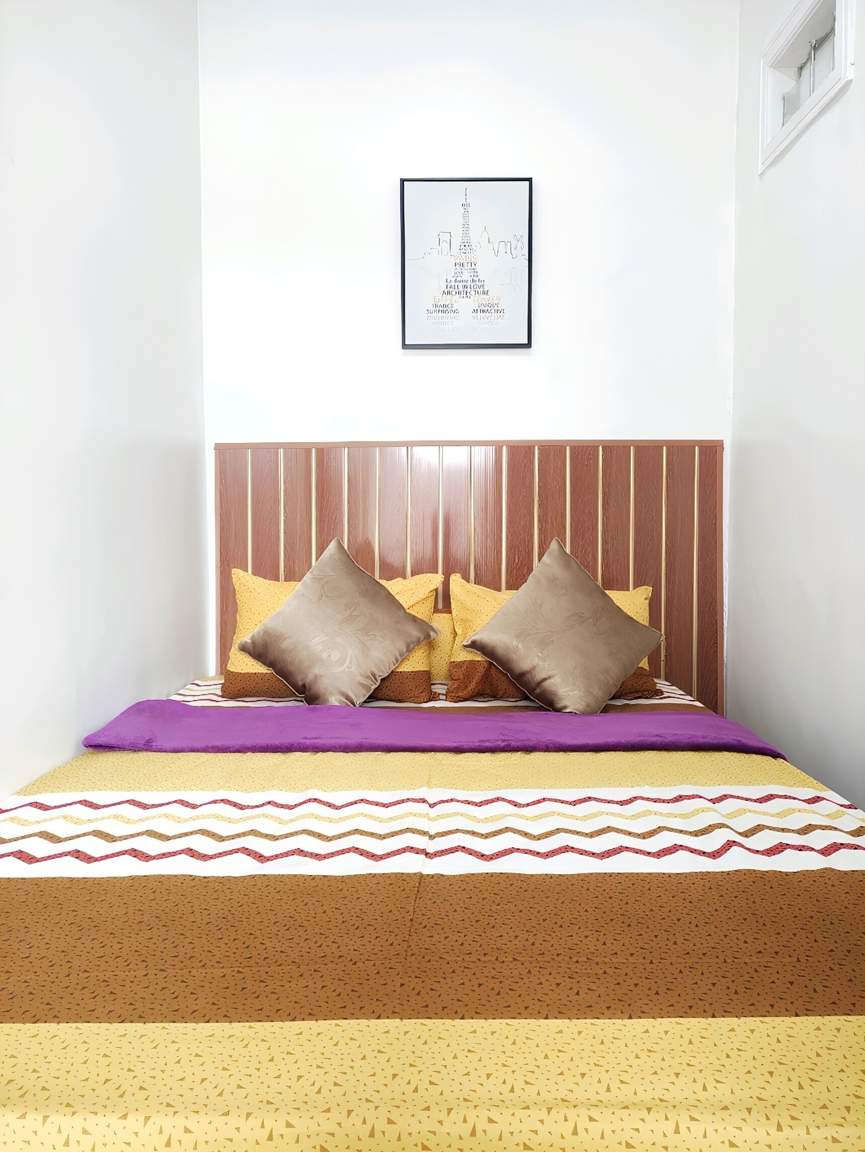 Uma cama bem arrumada com cabeceira listrada, uma citação emoldurada na parede e um edredom estampado.