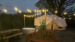 Uma tenda com área para dormir, um banco e uma pequena árvore.
