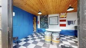Quarto com chão xadrez, paredes azuis e teto de madeira. Há uma mesa branca e banquetas listradas.