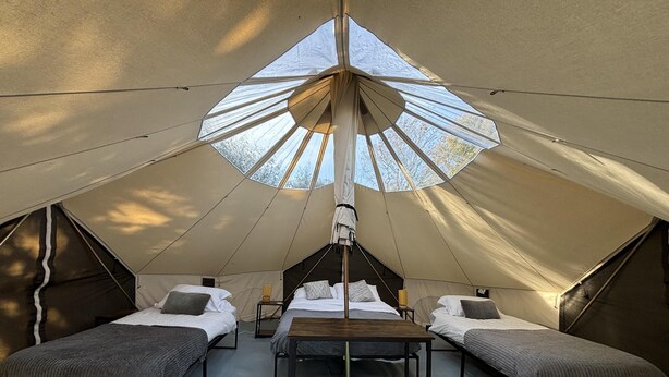 Uma tenda com três camas, uma mesa no centro e um toldo.