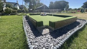 Piscina retangular com borda de madeira e de pedra, rodeada por grama e árvores.