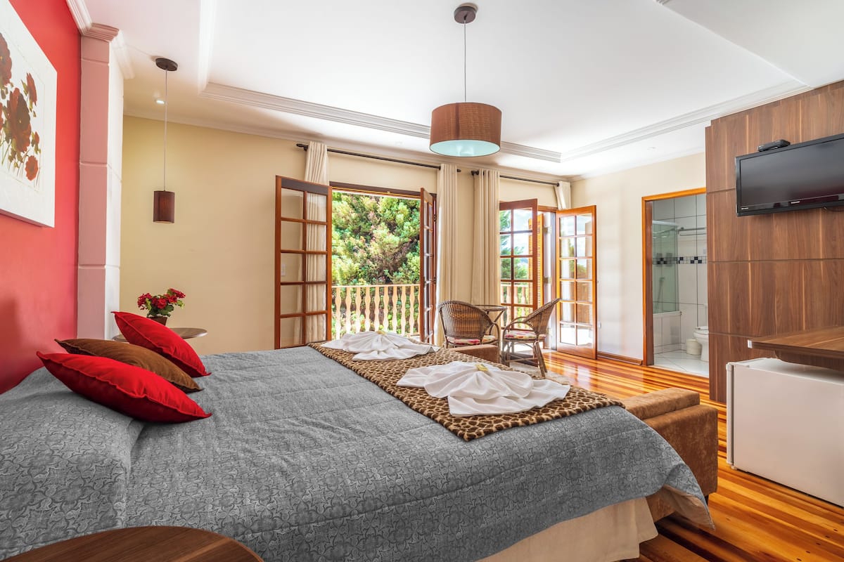 Quarto de hotel com cama, televisão, varanda e vista, além de área de chuveiro.