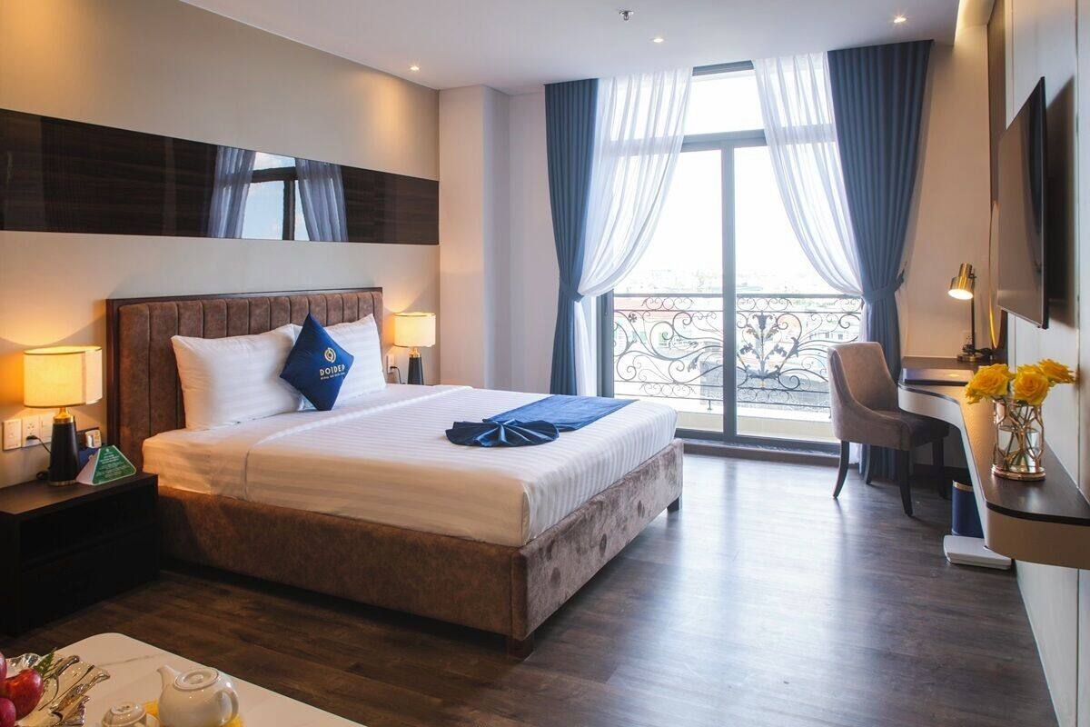 Quarto de hotel com uma cama grande, uma escrivaninha e varanda com cortinas.