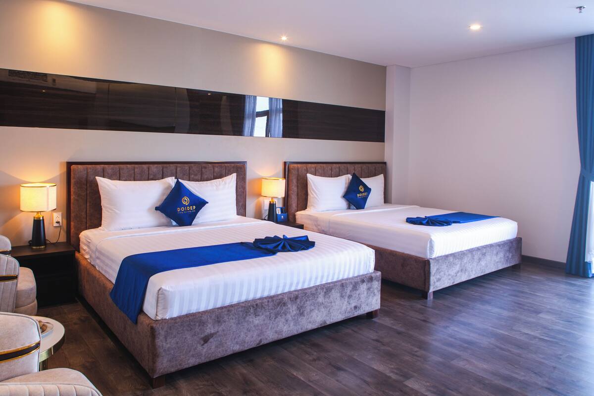 Quarto de hotel com duas camas, cada uma com cabeceira, mesas de cabeceira com luminárias e um espelho grande acima das camas.