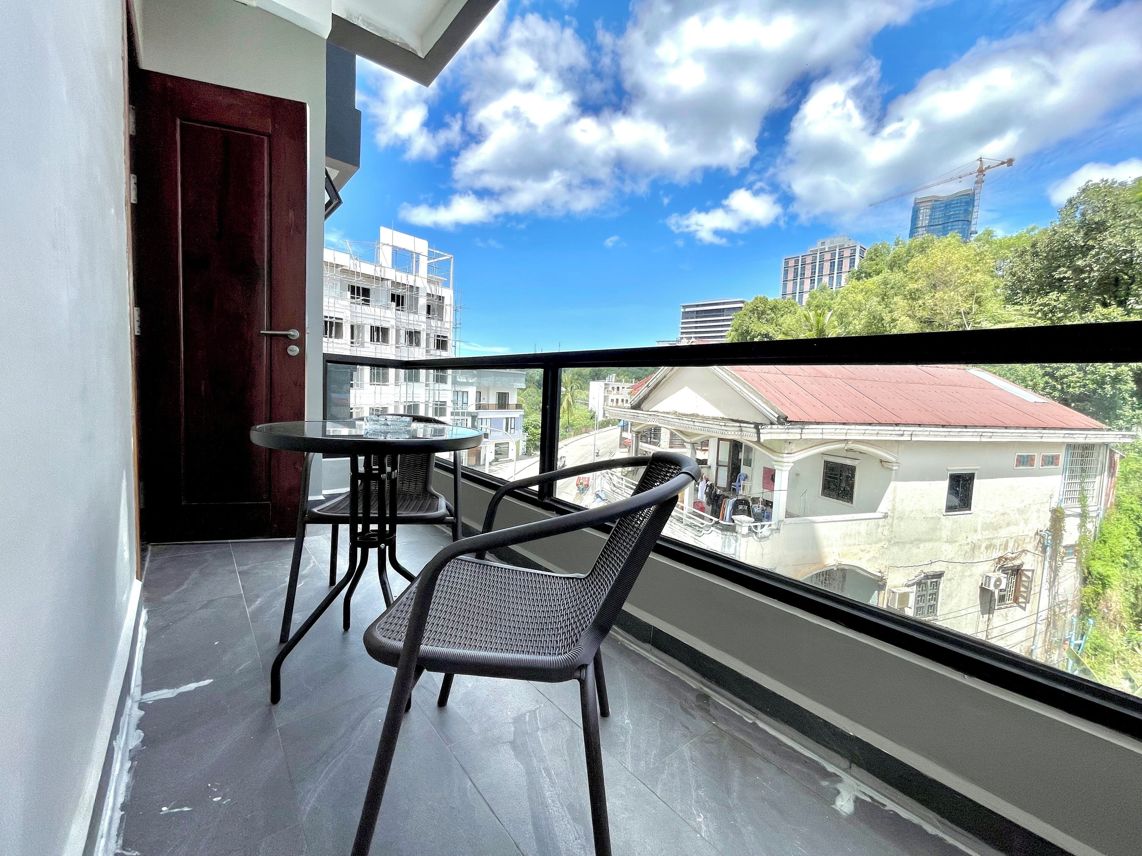 Uma varanda com mesa e cadeiras, uma porta e vista para edifícios e árvores.
