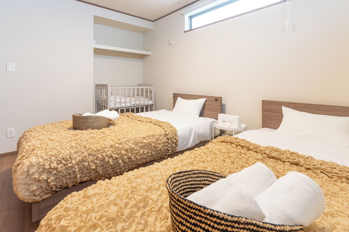 Quarto de hotel com duas camas, um berço, uma mesa pequena e uma janela.