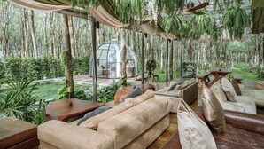 Um espaço amplo e arejado com um sofá grande, estrutura envidraçada e plantas pendentes.