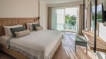 Quarto de hotel com uma cama grande, cabeceira de madeira e varanda com vista para o verde.