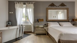 Quarto com cama grande, mesa de cabeceira, cômoda, banheira e espelho.