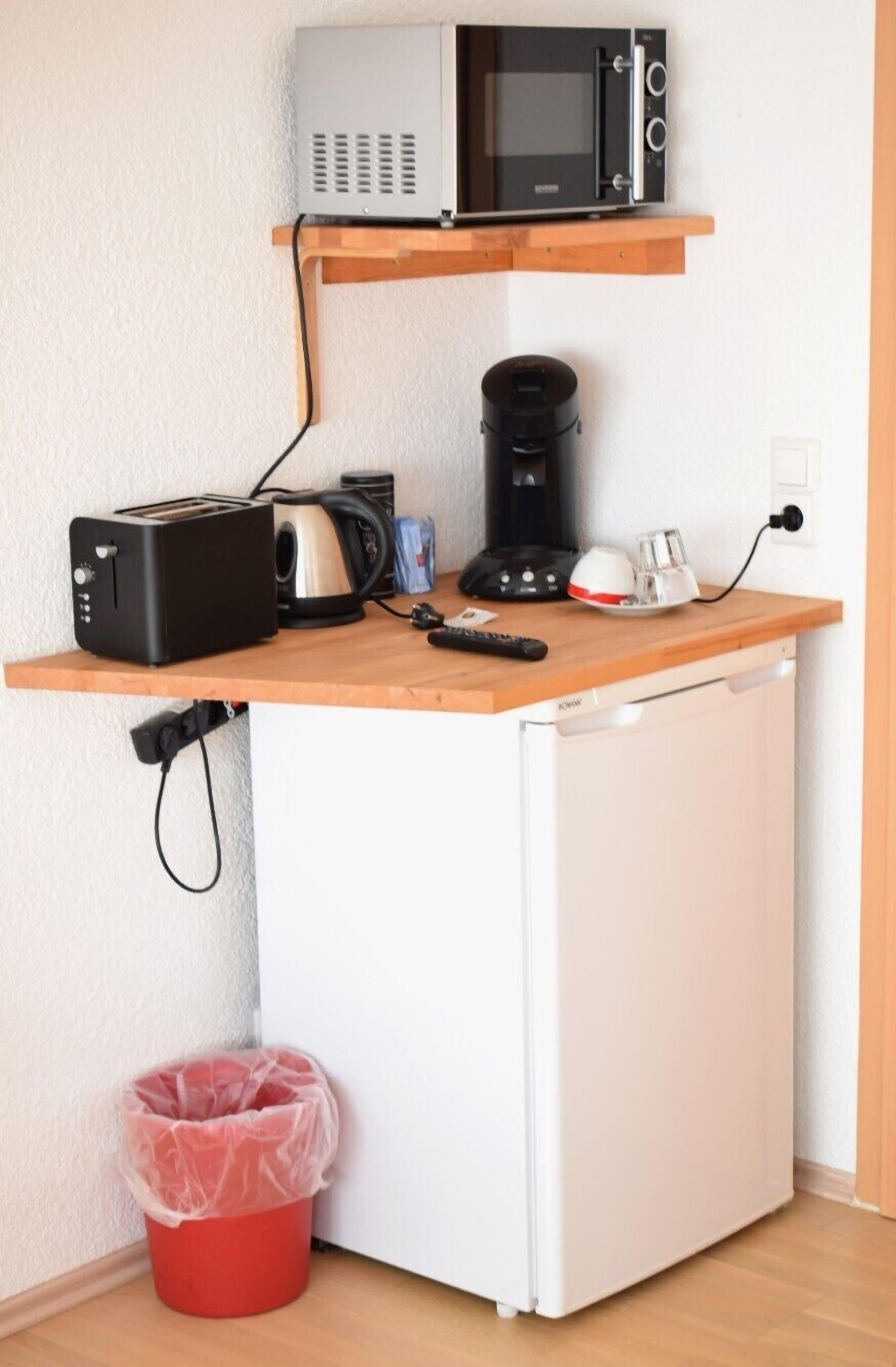 Uma cozinha compacta equipada com micro-ondas, torradeira, máquina de café e um refrigerador pequeno.