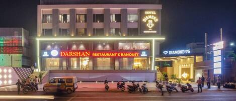 Um hotel com uma placa indicando 'Hotel Diamond 26', uma placa 'Darshan Restaurant & Banquet' e algumas motocicletas estacionadas na frente.
