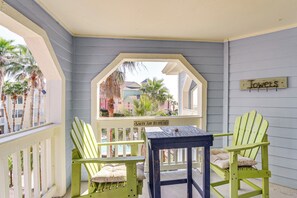 Varanda com duas cadeiras Adirondack verdes, uma mesa pequena e uma placa com a inscrição 'Salty Air Retreat'.